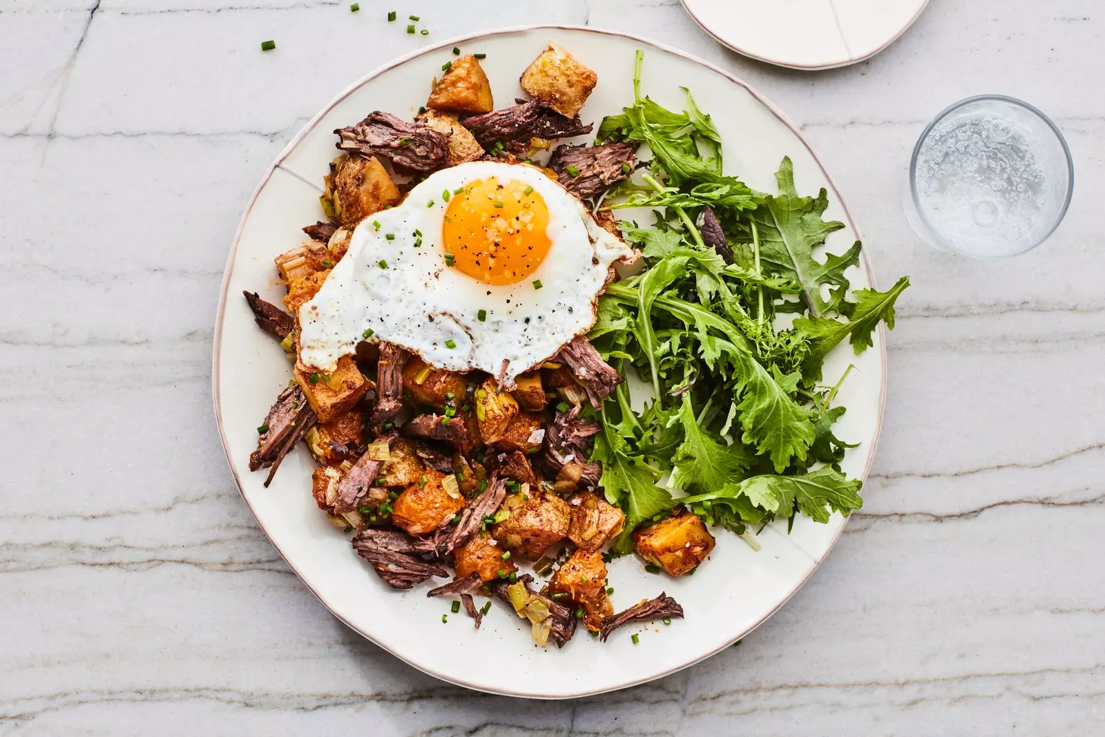 Plaat van gestoofd rundvlees ontbijt hash met eieren en een salade op een teller.