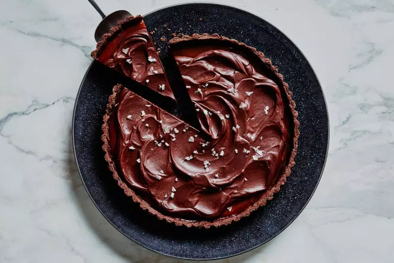 Eine einzelne Scheibe, die von einer Torte entfernt wird, die mit Swoops und Strudeln aus Schokoladenganache belegt ist.