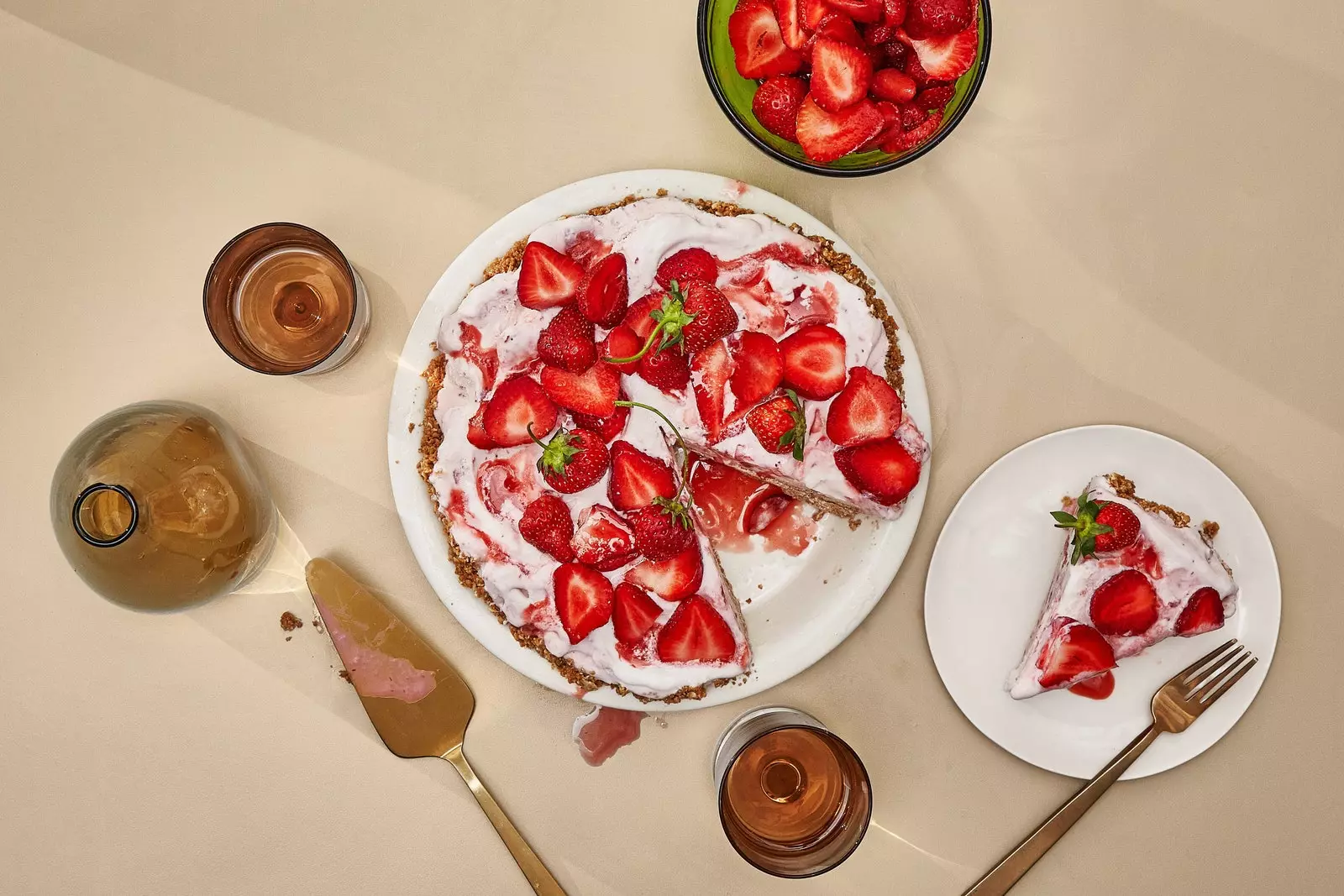 Overhead-bilde av en kremfylt pai toppet med skivede jordbær med én skive fjernet på en tallerken.