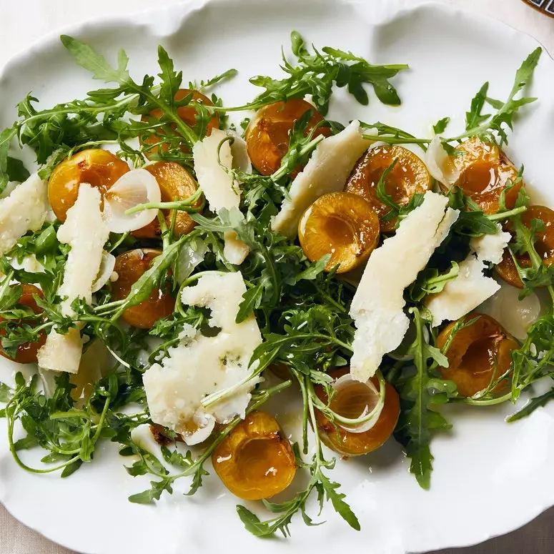 En vit oval tallrik med ruccola italienska plommon och parmesanost.