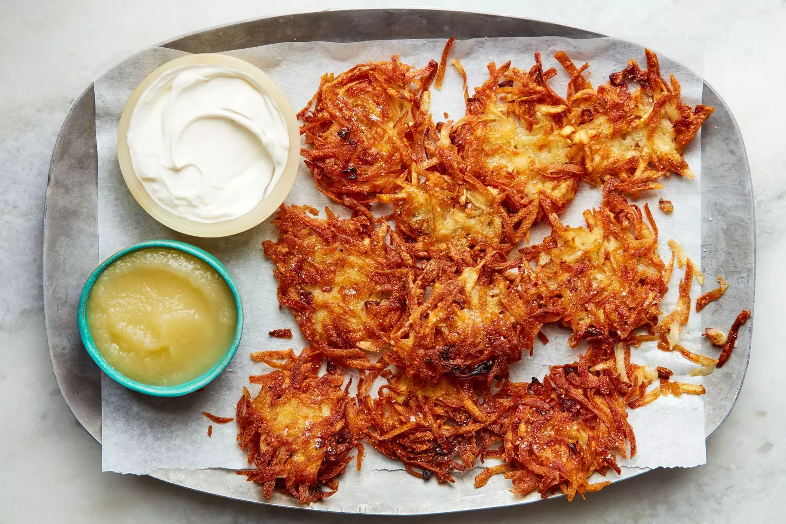 Foto vun Latkes op engem Déngschtplack mat Schësselcher vun Äppel a Sourcreme op der Säit.