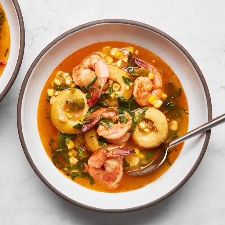 Foto di due ciotole di zuppa di chochoyotes con gamberetti su un ripiano di marmo con un cucchiaio.