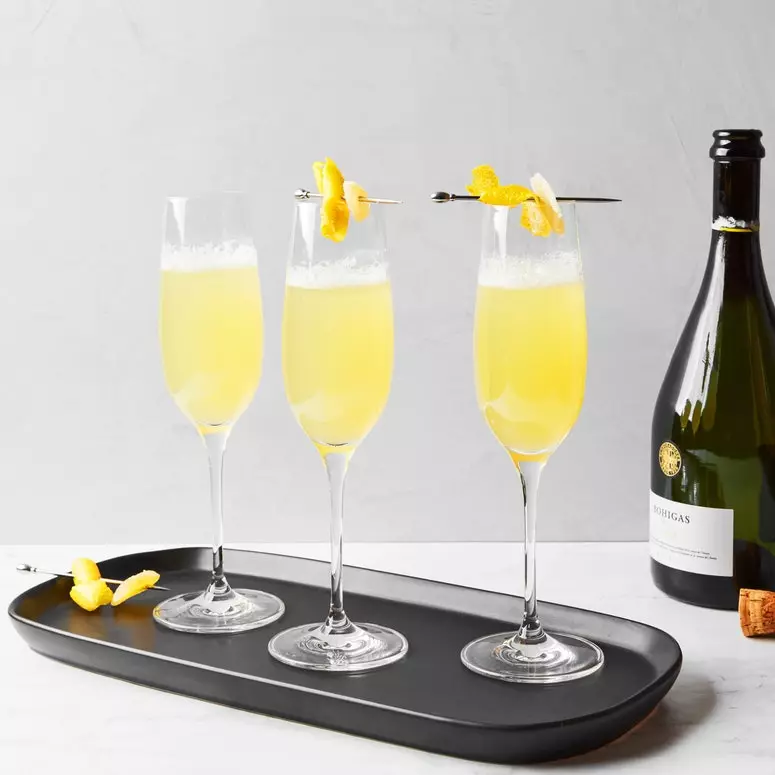 Fotografie cu trei pahare de Fleming Fizz cu garnituri de coajă de lămâie și o sticlă de șampanie.