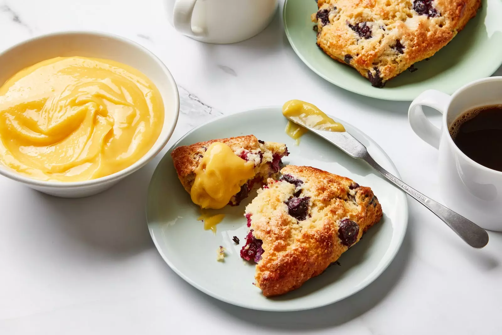 Foto van bosbessenscones met citroengestremde melk en koffie aan de zijkant.