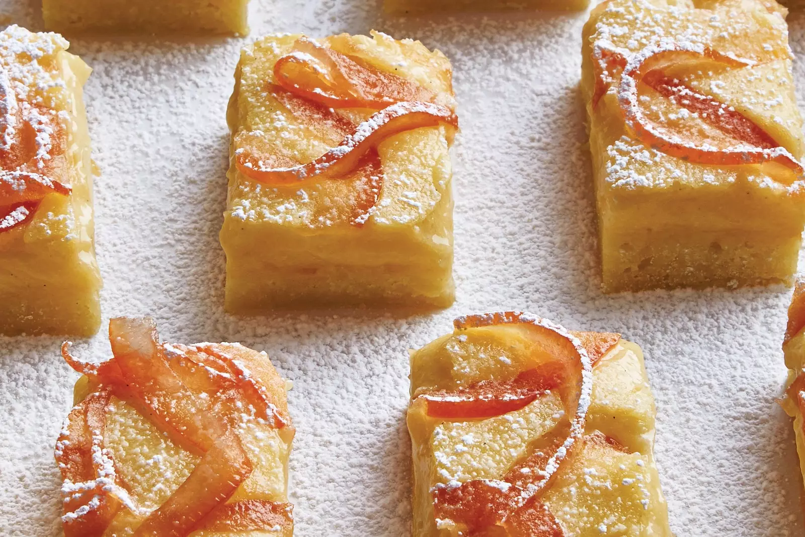 Filas de barras cítricas amarelas brillantes cubertas con reladura de pomelo confitada e espolvoreadas con azucre en po.