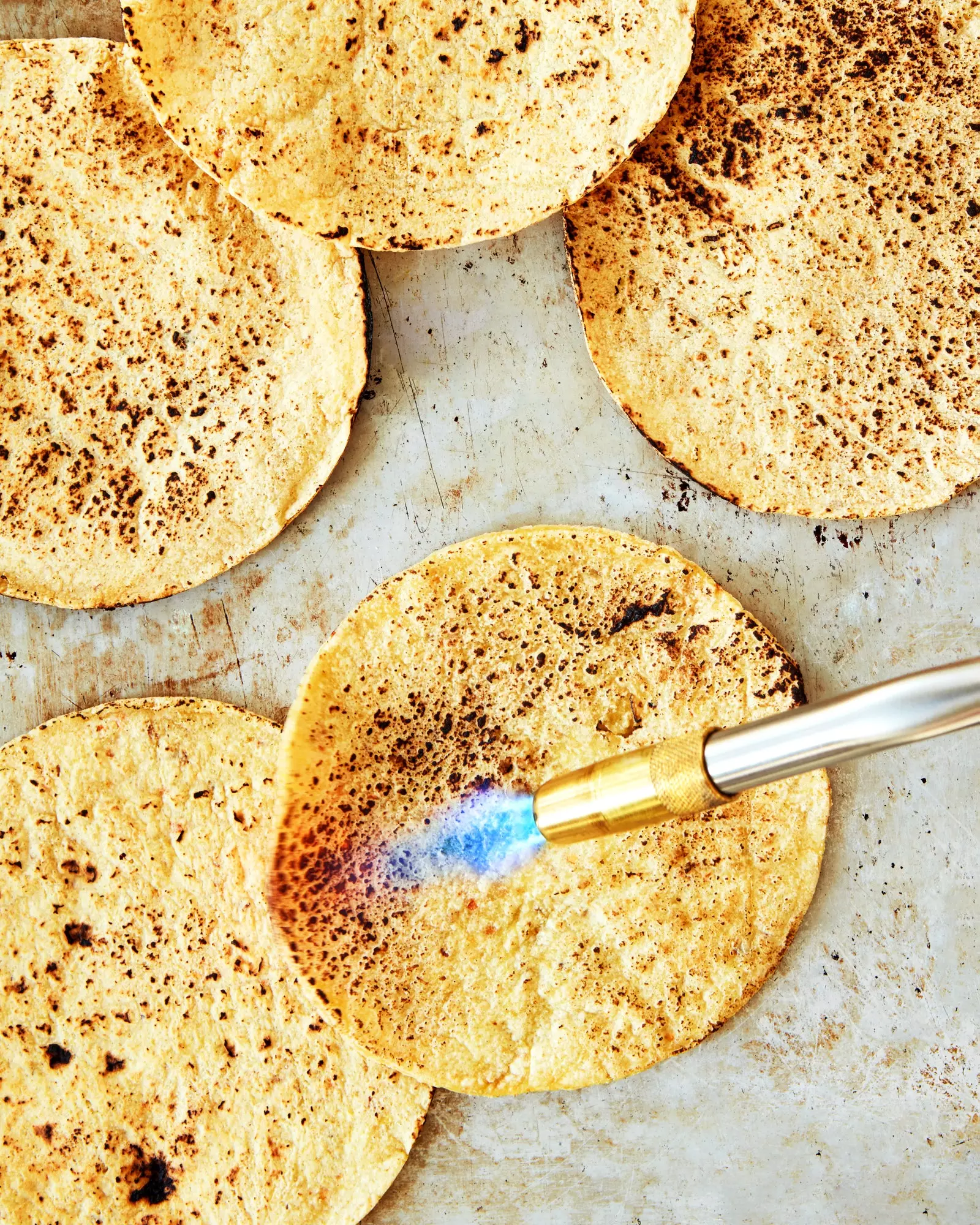 Foto de um maçarico carbonizando tortilhas de milho em uma assadeira.