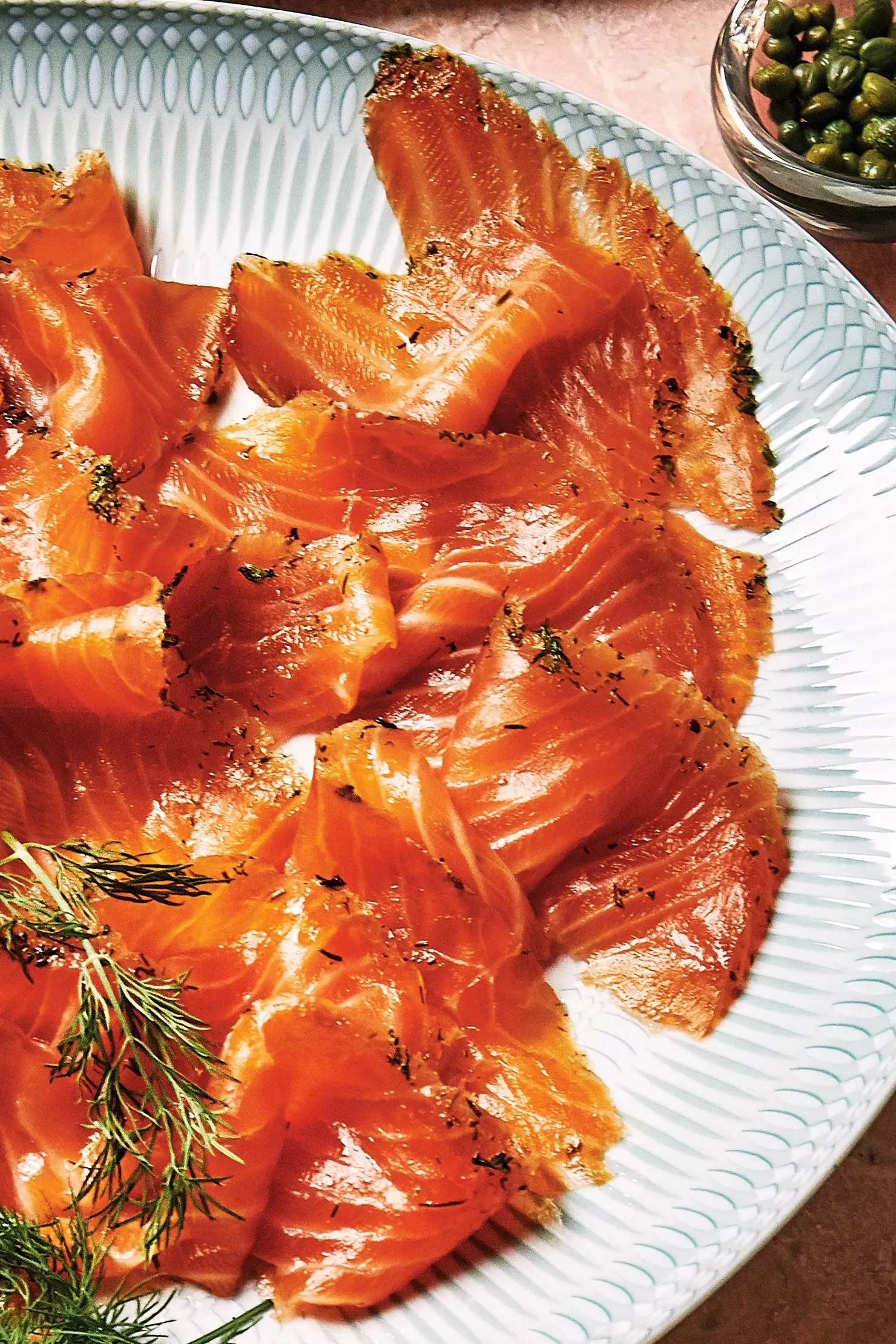 Irisan ipis salmon kapok vibrant dina piring porsi disusun kalawan capers dill bawang beureum sarta leuwih.