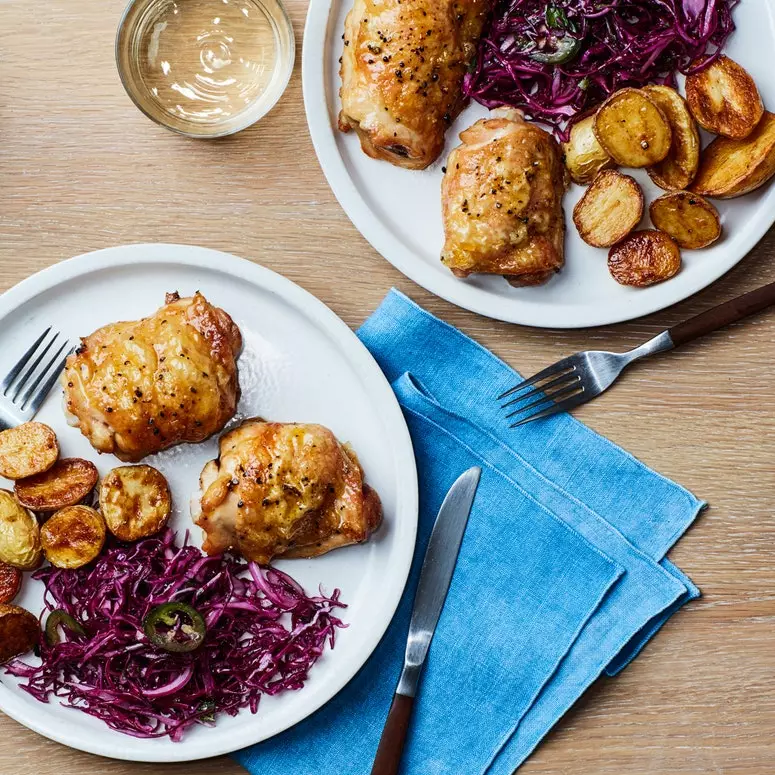 Knuspriges Hühnchen und Kartoffeln mit Krautsalat auf zwei weißen Tellern mit blauen Servietten an der Seite.