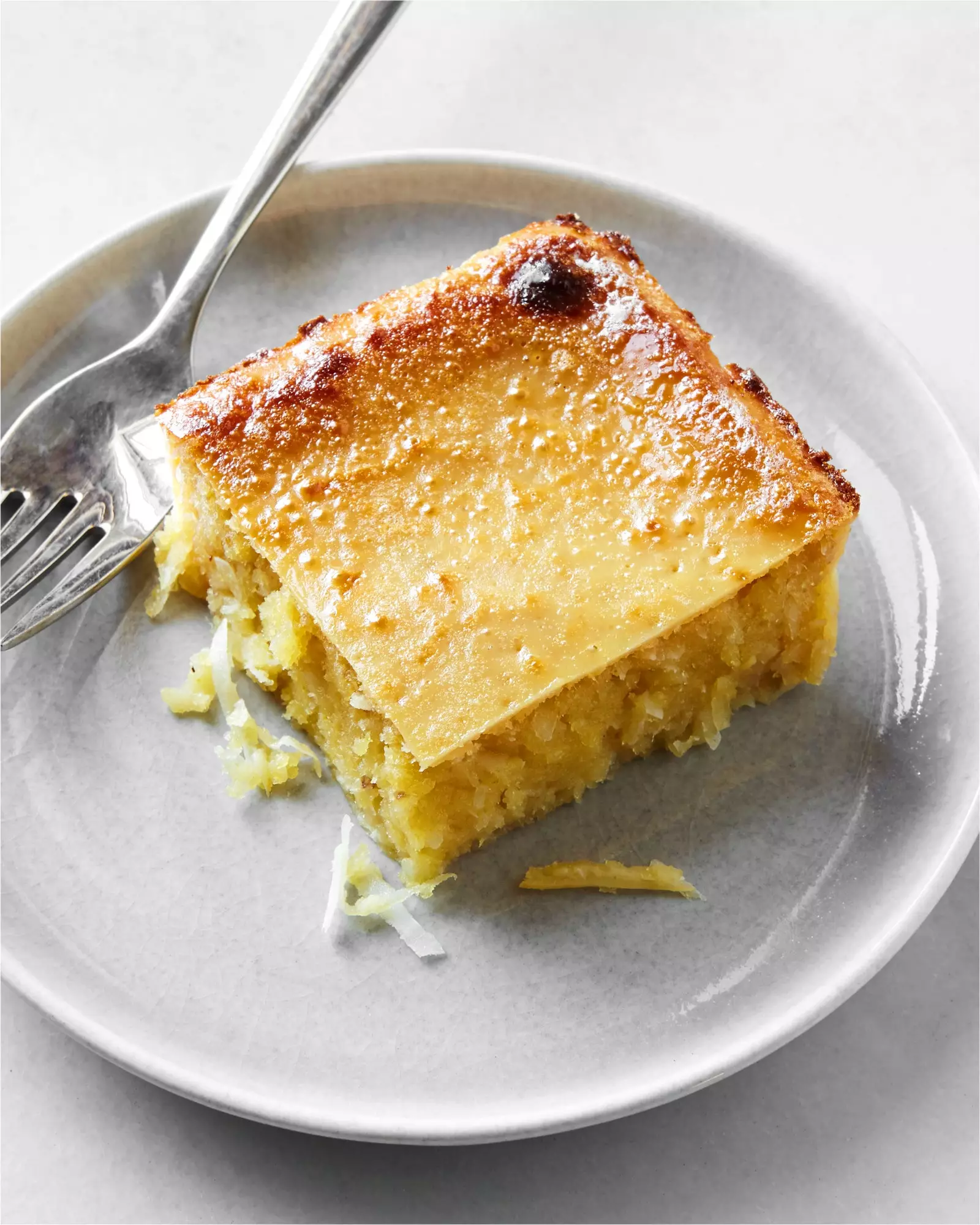 Foto de um pedaço de bolo de mandioca em um prato com um garfo.