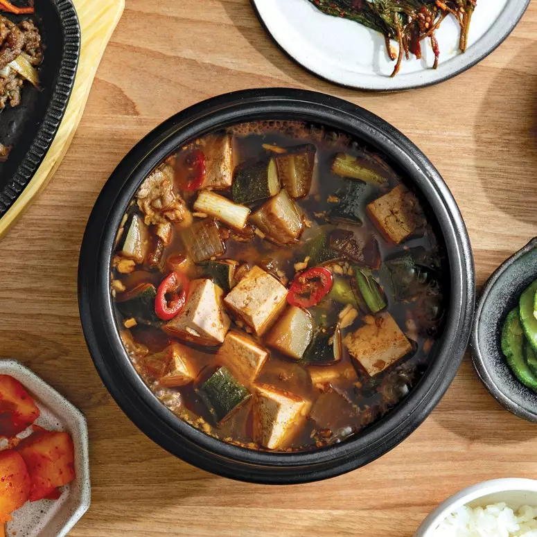 Koreanische Rezepte Foto von fermentiertem Sojabohneneintopf aus Hooni Kims „My Korea“, umgeben von geschnittenen Gurken, Seetangreis …