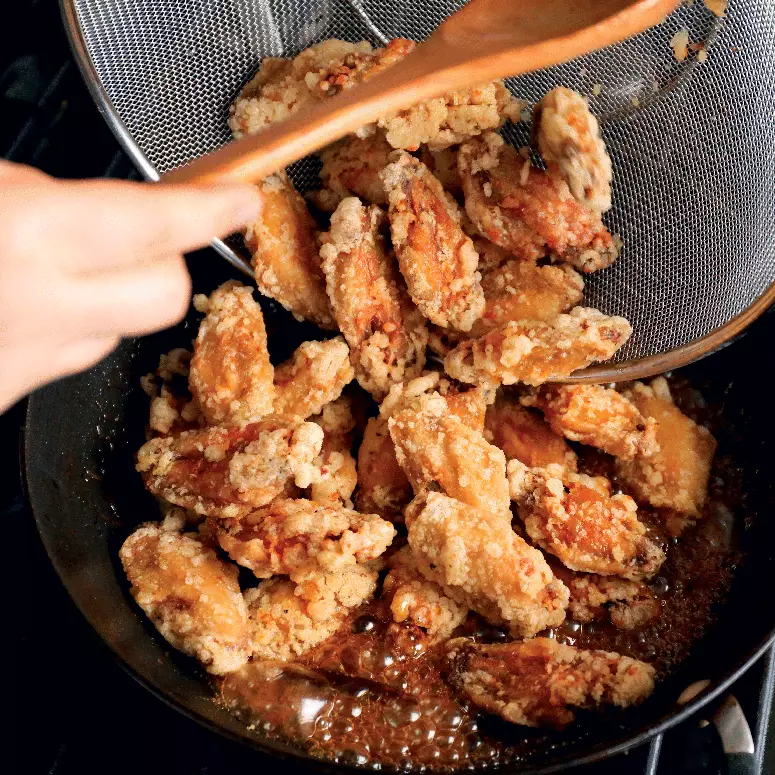 Pollo frito coreano pasando de un colador a una sartén de salsa burbujeante.