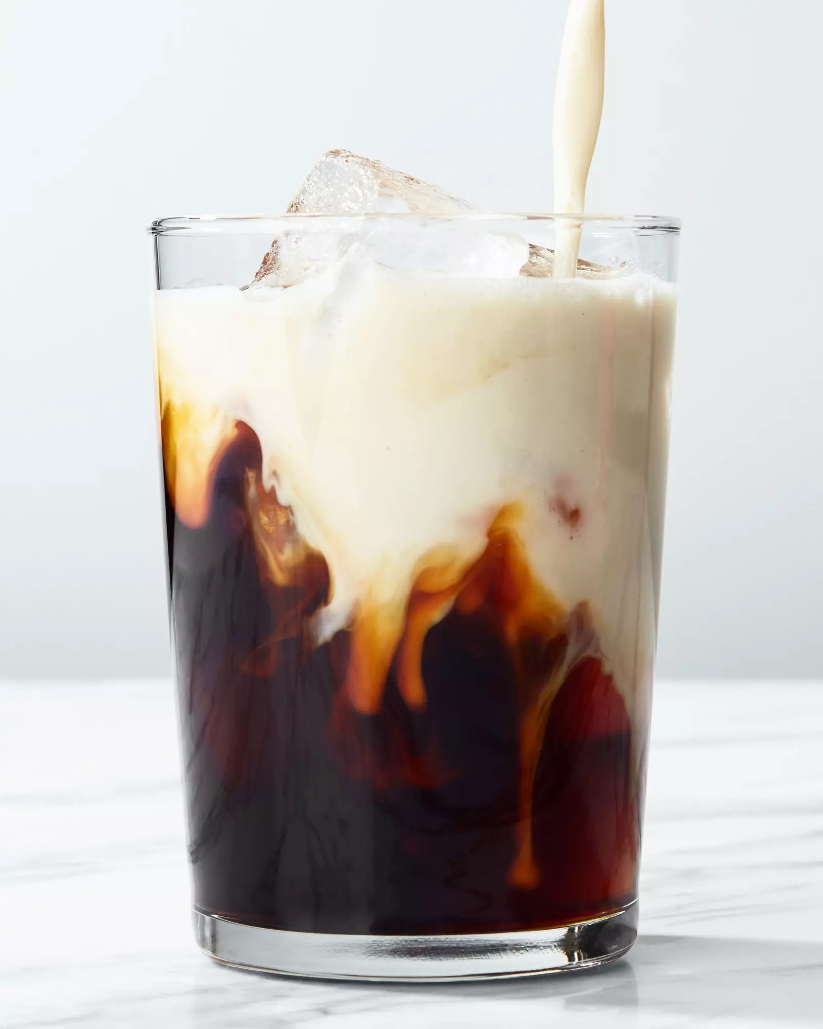 Foto e qumështit të tërshërës duke u derdhur në një gotë kafeje të ftohtë.