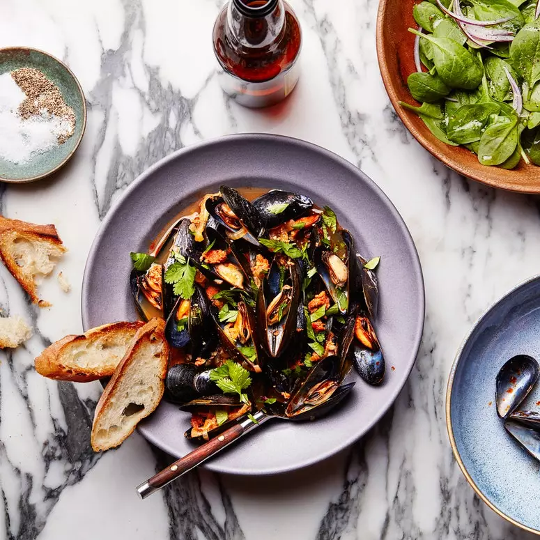 Mejillones al vapor de cerveza con chorizo y rebanadas de baguette en un tazón poco profundo.