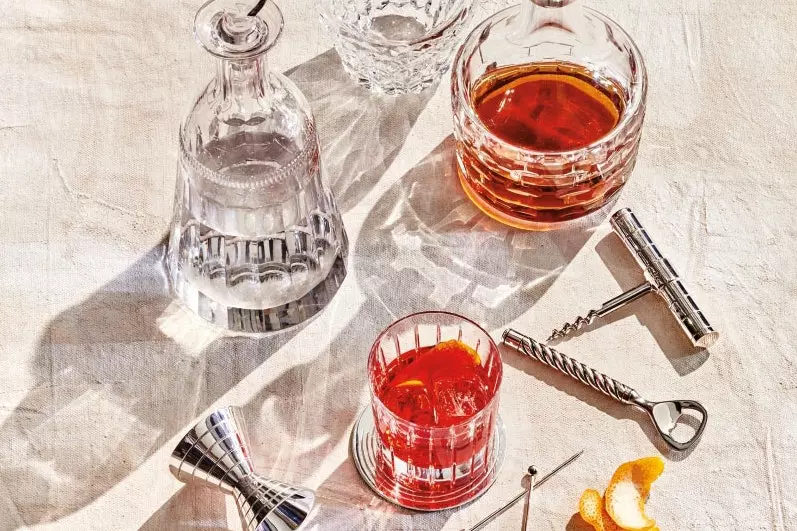 Foto van bargereedschap waaronder een glas met een cocktail een jigger een flesopener en kristallen flessen gevuld met sterke drank.