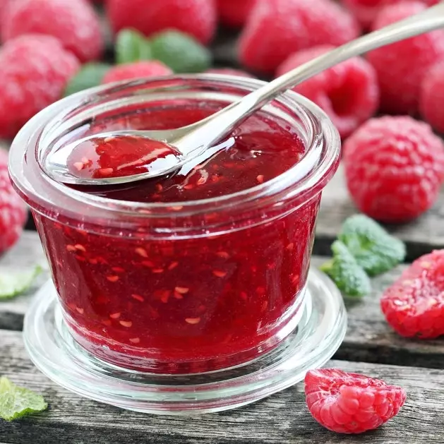 Vasetto di marmellata di lamponi con cucchiaio sul tavolo da picnic con lamponi freschi.