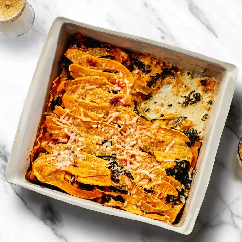 Gratin mit Butternusskürbis und Rahmspinat in einer Schüssel mit einer herausgenommenen Portion und einem Glas Wein als Beilage.