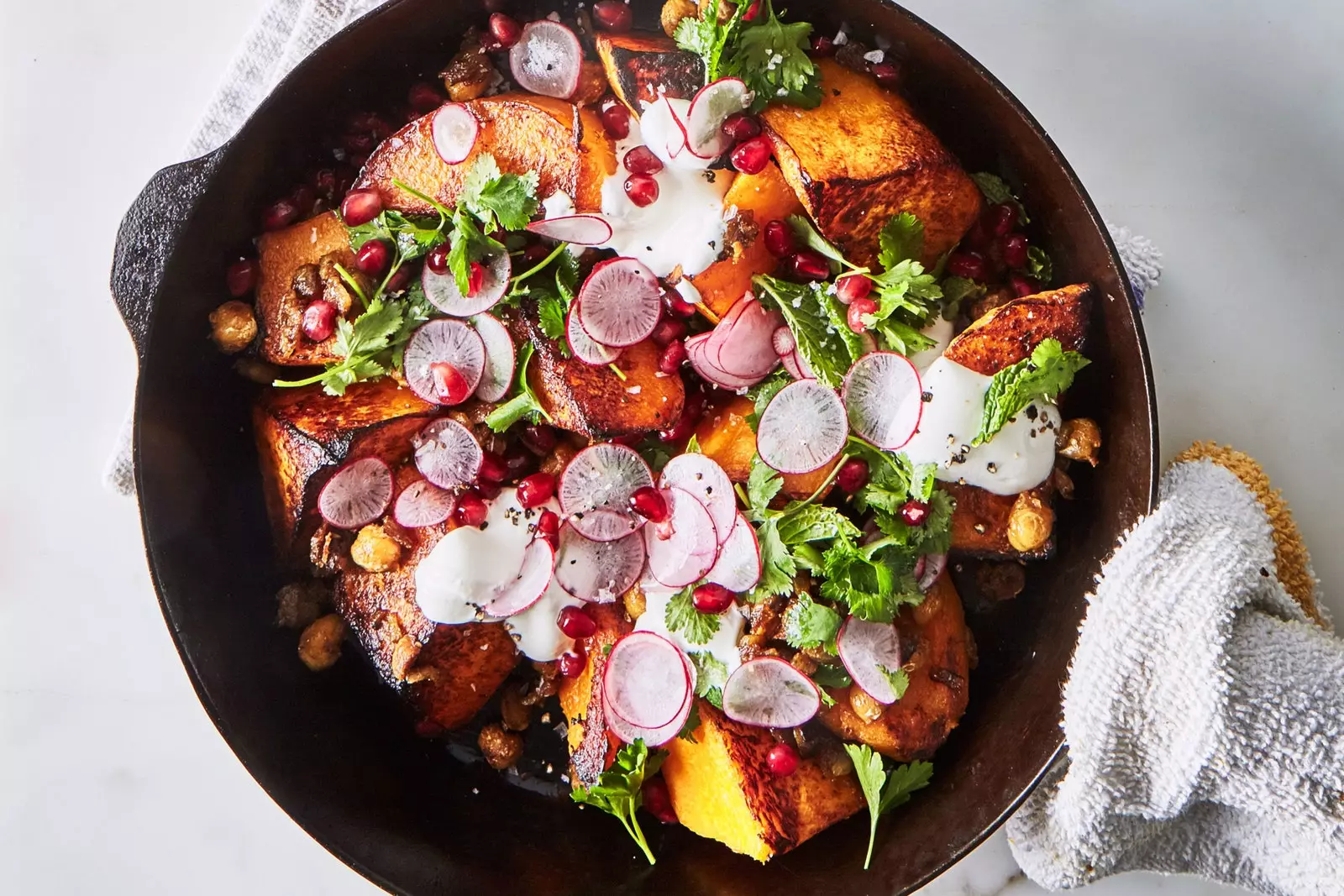 Eine Pfanne gefüllt mit mit Butternusskürbis gewürzten Kichererbsen, garniert mit Radieschen und Kräutern.