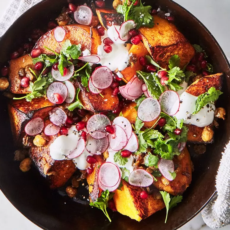 Een koekenpan gevuld met butternut squash gekruide kikkererwten gegarneerd met radijs en kruiden.