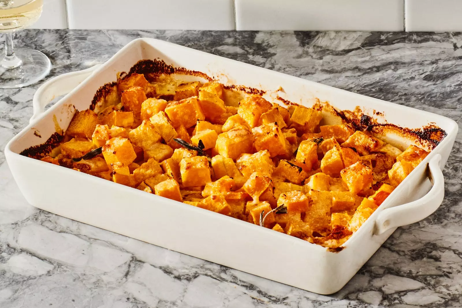 Parmesan Roasted Butternut Squash ໃນຈານພ້ອມຈອກເຫຼົ້າແວງຂາວຢູ່ຂ້າງ