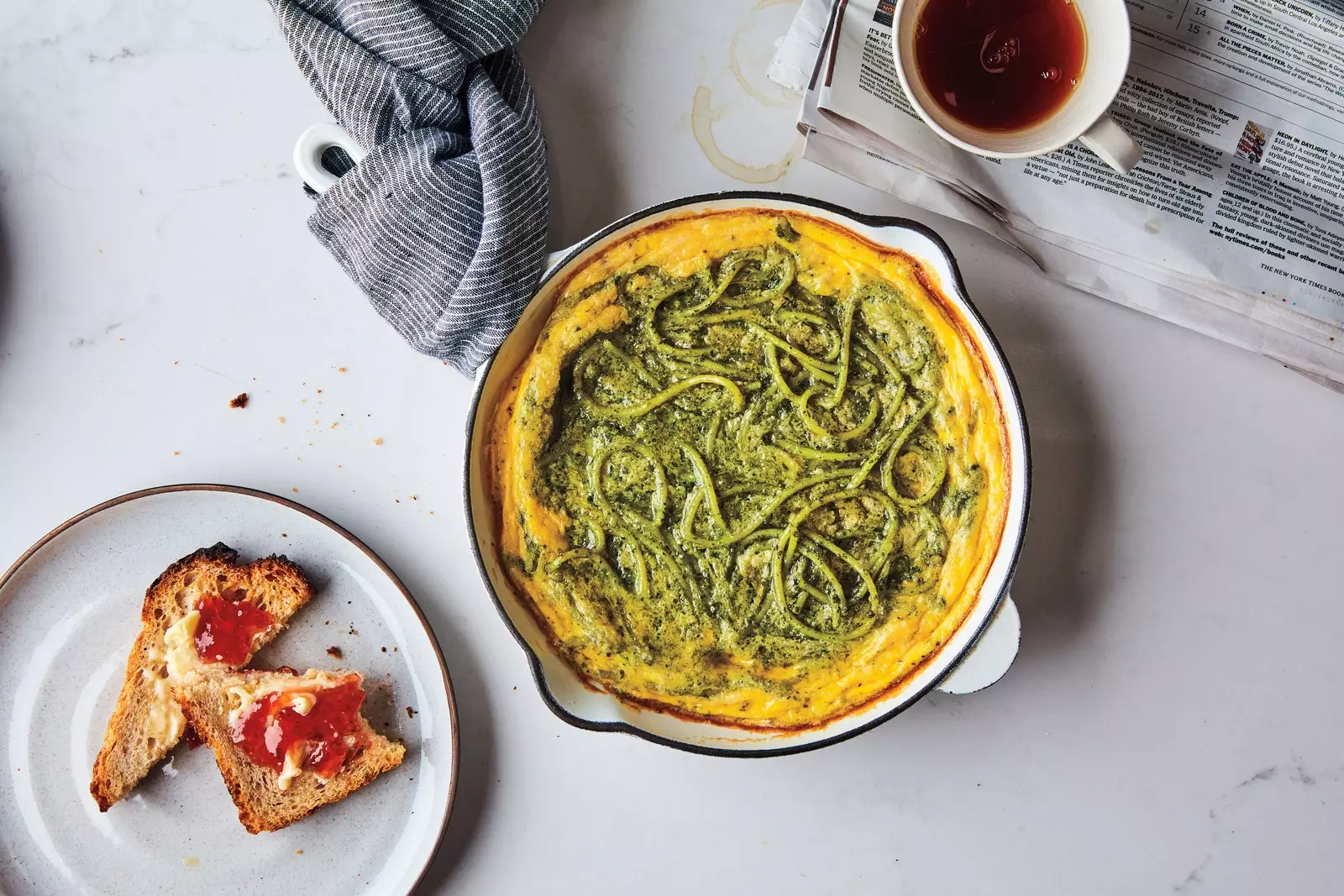 Ukubuka okuphezulu kwe-pesto pasta frittata esitsheni sokubhaka esinohlangothi lwe-toast.