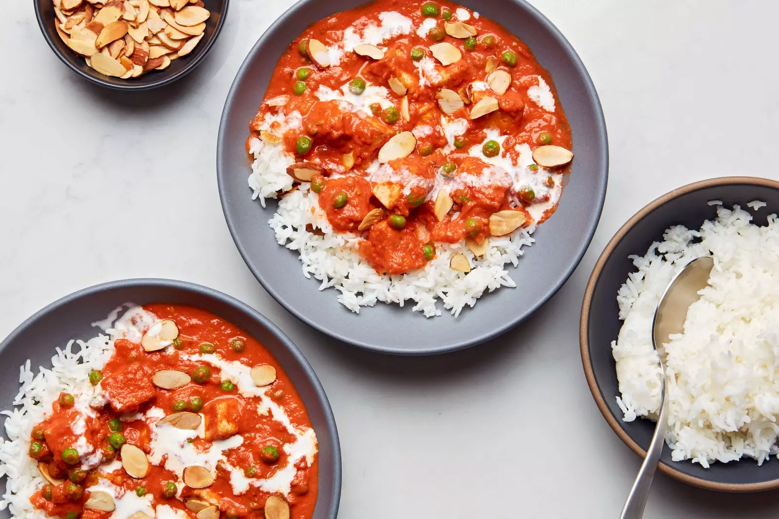 Foto von zwei Schüsseln Butter Paneer mit weißem Reis und Mandelblättchen an der Seite.