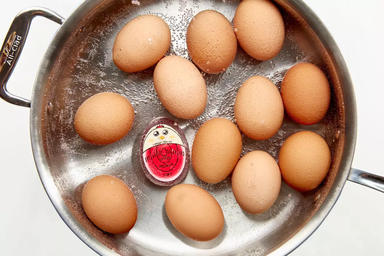 Foto de um temporizador de ovo Noble Egg em uma panela de água fervente com uma dúzia de ovos.