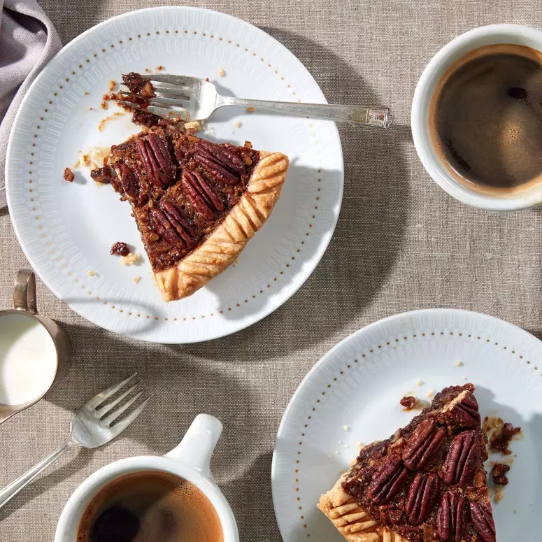 Skivor av pekannötspajer på tallrikar med koppar kaffe på ett bord.