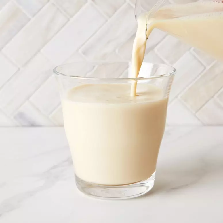 Foto de leite de soja sendo despejado em um copo em uma bancada de mármore.