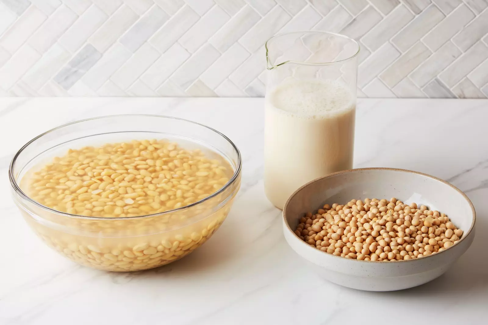 Fotografija čaše sojinog mlijeka, zdjela sojinog zrna i zdjela sojinog zrna koji se namaču u vodi.
