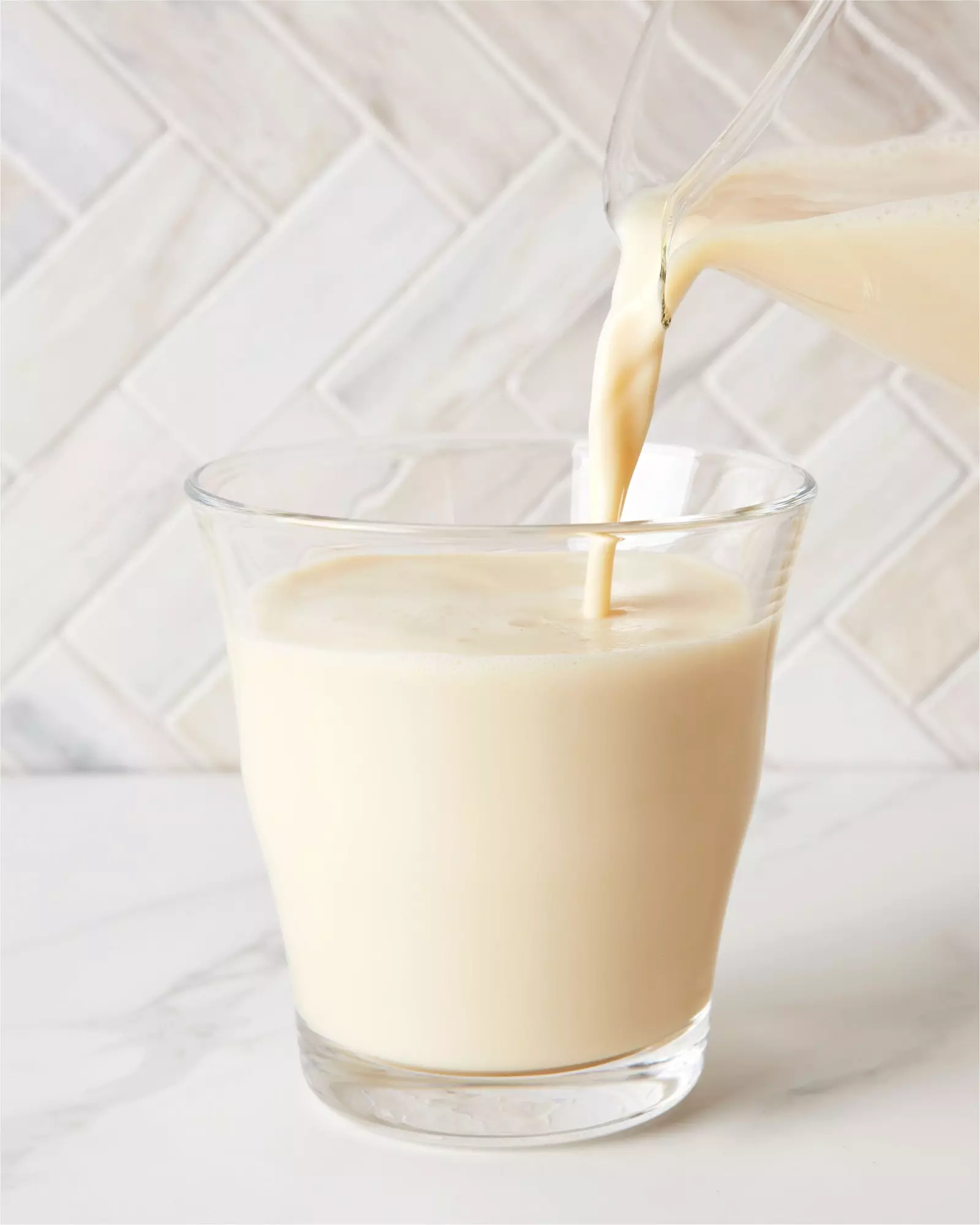 Zdjęcie mleka sojowego wlewanego do szklanki na marmurowym blacie.
