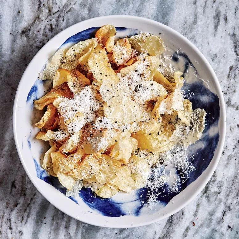 Patatas fritas cubiertas con queso rallado y pimienta recién molida en un bol estampado en azul y blanco.