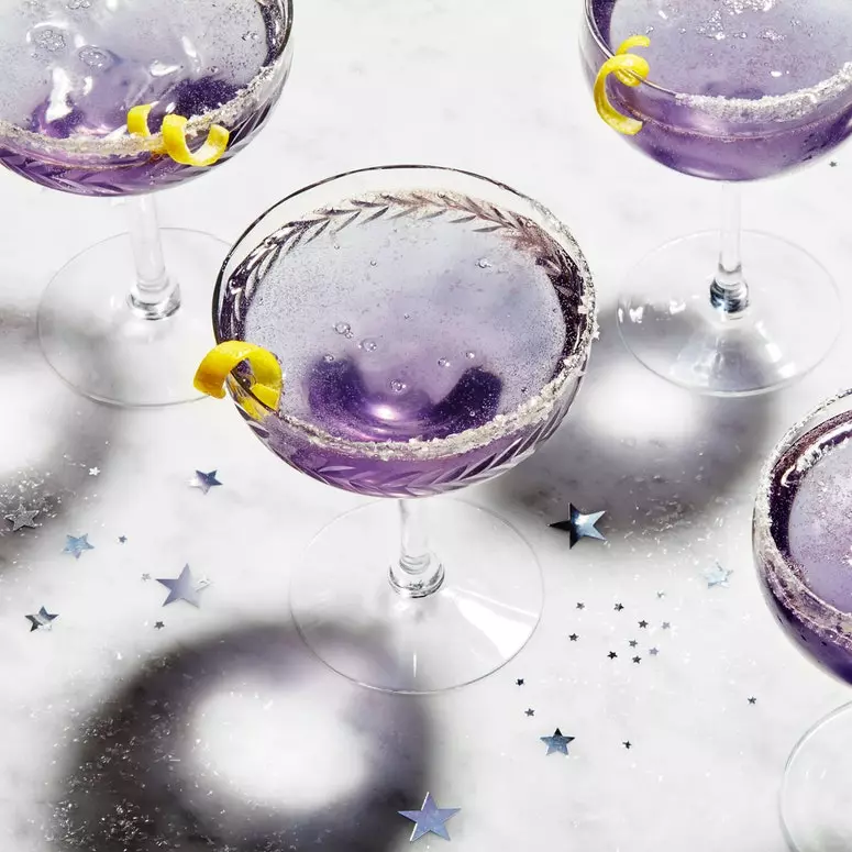 Foto von vier Cocktailgläsern, gefüllt mit einem violetten Cocktail und kleinen Zitronenspiralen.