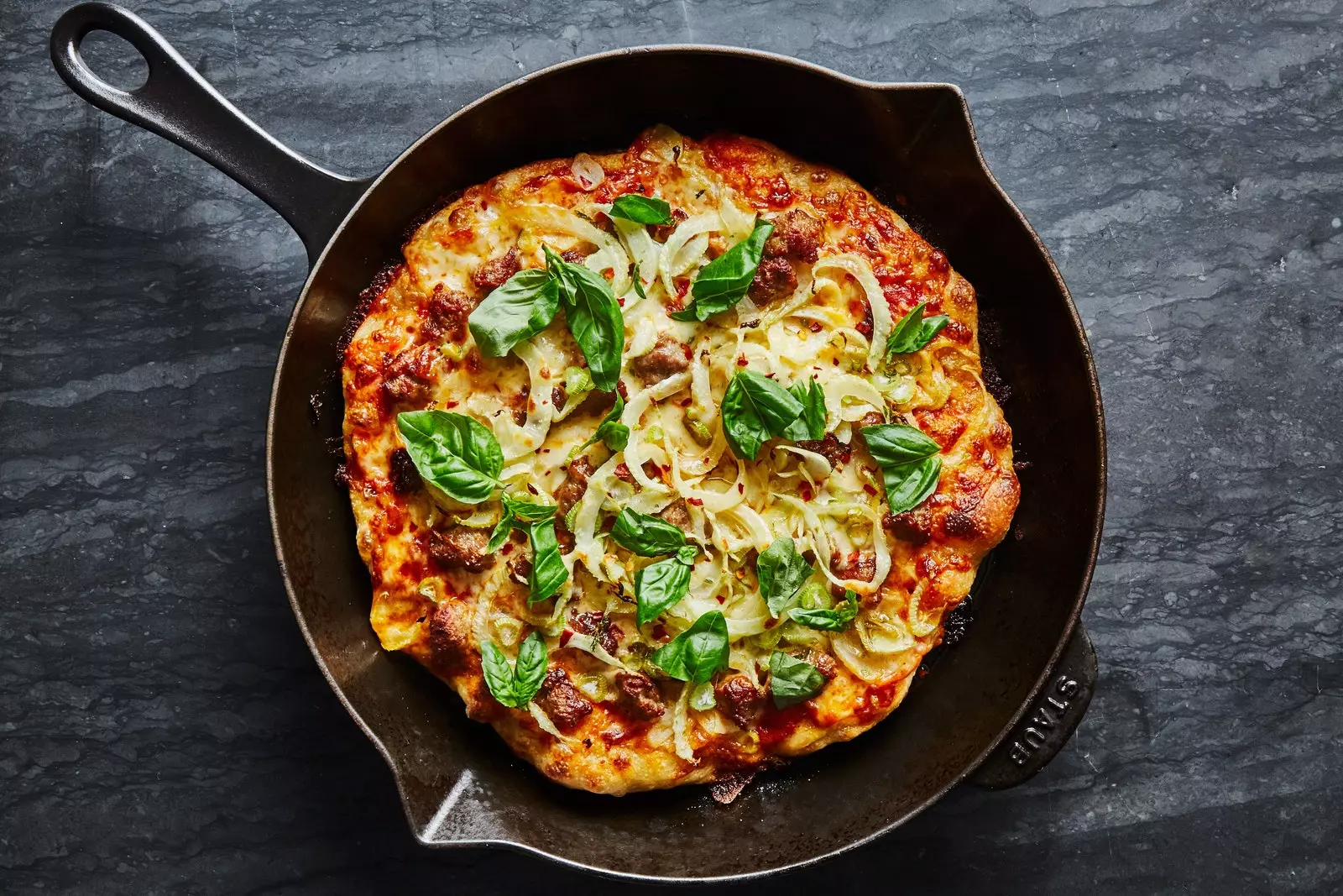 Foto af vores støbejerns pizzaopskrift toppet med fennikel og pølse vist i stegepanden.