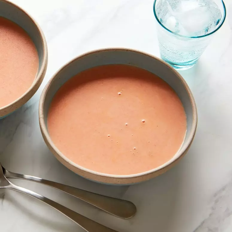 Снимка на две купи кремообразна доматена супа на Edna Lewis с две лъжици и чаши вода отстрани.