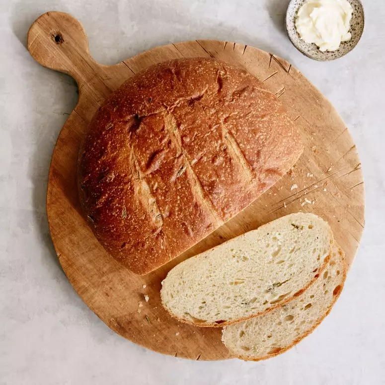 Hogaza de pan de aceite de oliva de romero con una rebanada cortada en una tabla circular de madera.