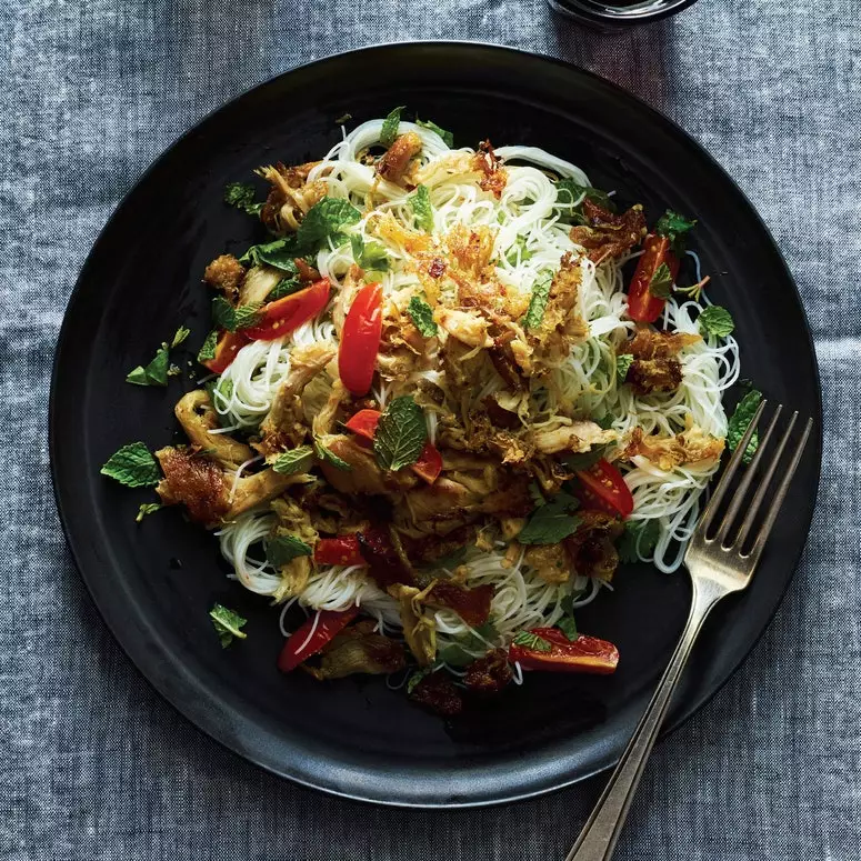 Øverst set kyllingeconfitering med syltede tomatløg og risnudelsalat på en sort tallerken.