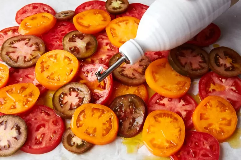 Salah satu dispenser minyak zaitun terbaik menuang minyak ke atas tomato.