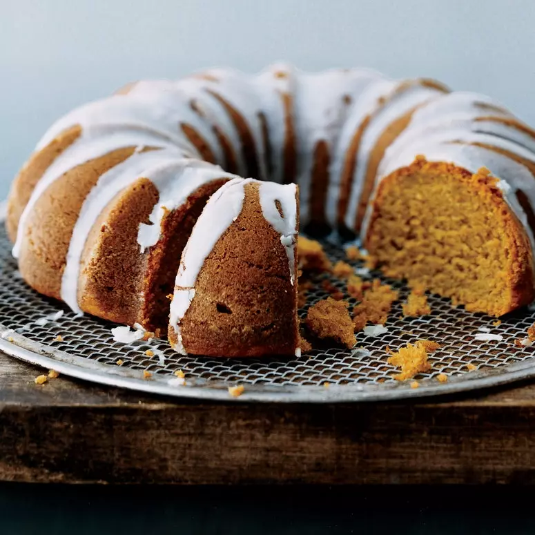 Pumpkin spice bundt ncuav mog qab zib topped nrog dawb icing rau ntawm ib tug txias khib.