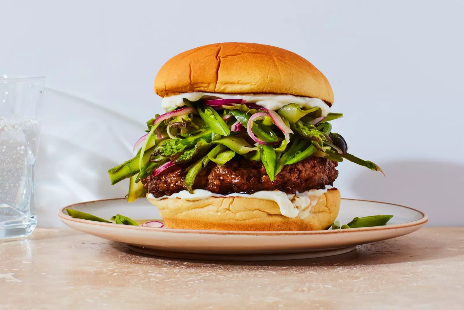 Una vista laterale di un hamburger su un piatto un panino soffice di patate con salsa di yogurt gocciolante spalmato su entrambi i lati l'hamburger è...