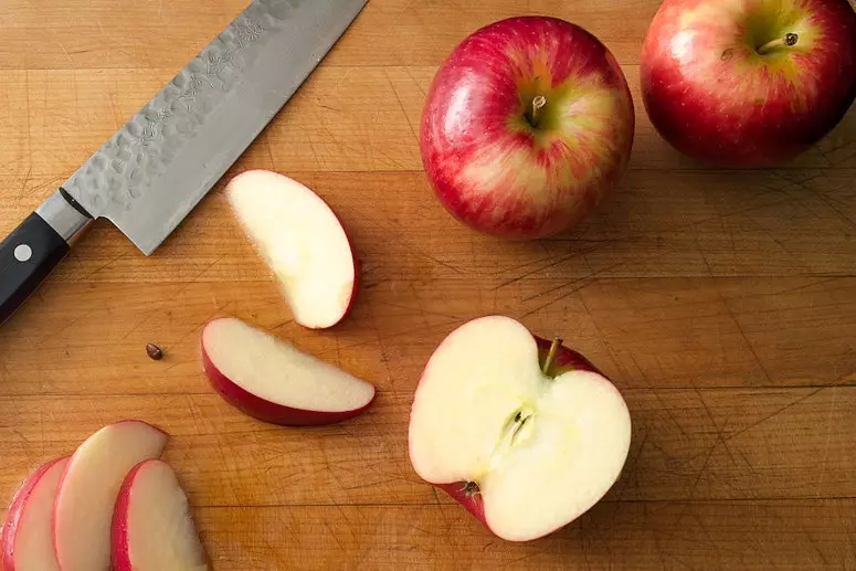 Slika narezanih surovih rdečih jabolk in noža na deski za rezanje, da pokažete, kako preprečiti, da jabolka porjavijo.