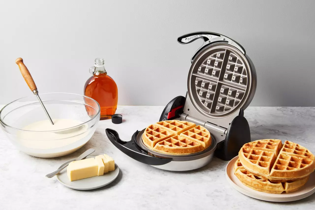 Foto Pembuat Wafel Presto di atas meja marmer dengan wafel Belgia, adonan, mentega, dan sirup maple.