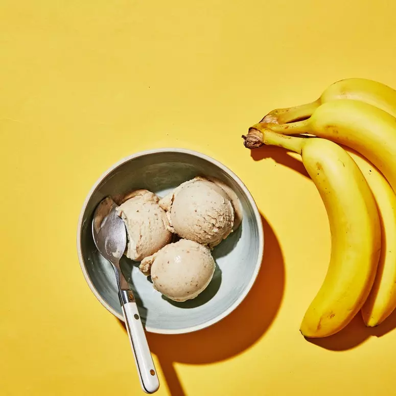 ငှက်ပျောသီးစည်းဘေးမှာ ဇွန်းတစ်ချောင်းနဲ့ vegan ငှက်ပျောသီးရေခဲမုန့် သုံးခွက်စာ။