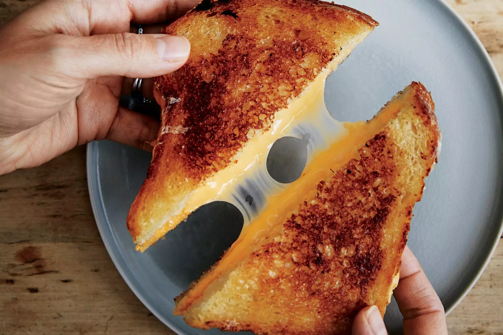 Due mani che separano le metà tagliate in diagonale di un panino al formaggio grigliato.