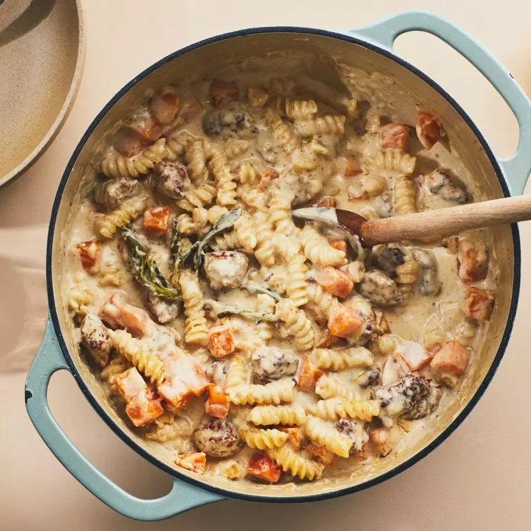 Un tir de dalt de pasta cremosa d'una olla amb botifarra i carbassa amb una cullera de fusta a l'olla.