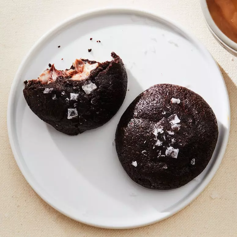 Biscuits brownie à fond noir garnis de sel feuilleté sur une assiette avec une bouchée de l'un des biscuits.