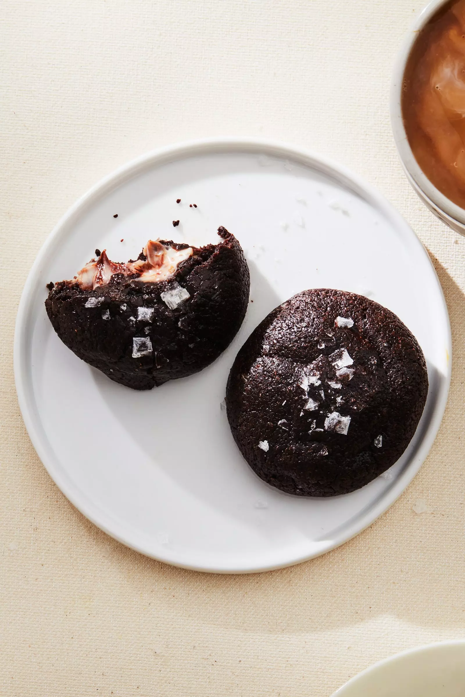 Biscuits brownie à fond noir garnis de sel feuilleté sur une assiette avec une bouchée de l'un des biscuits.