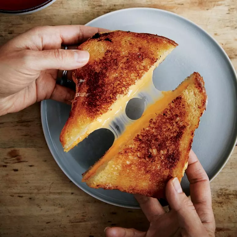 Dos manos separando mitades cortadas en diagonal de un sándwich de queso a la parrilla.