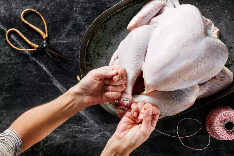 如何准备火鸡：一个人的手用厨房绳子把鸡腿绑在一起。