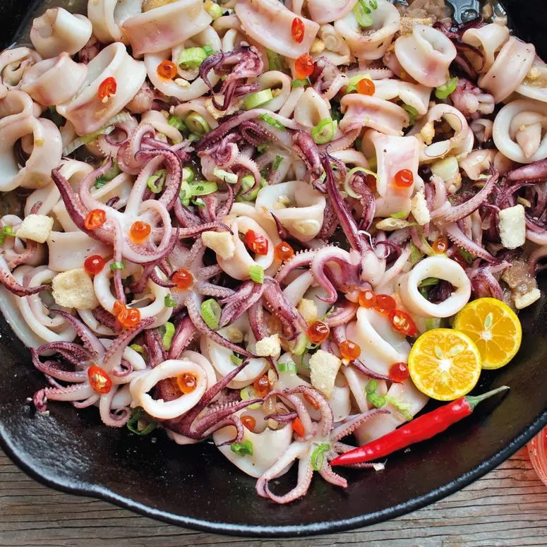 Mphete za squid zophikidwa ndi ma tentacles mu poto yachitsulo yokongoletsedwa ndi chile chofiyira ndi calamansi watheka.