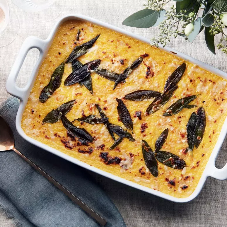 Cheesy Butternut Squash Polenta an engem wäisse véiereckege Bakform mat zwee Gedrénks an engem Portiounsläffel.